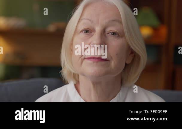 Thoughtful Senior Woman Looking At Camera In Cozy Home Interior ...