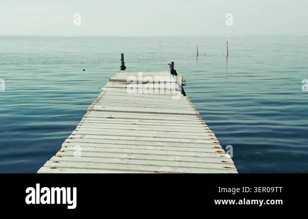 A serene and minimalist shot of a weathered wooden pier stretching into ...
