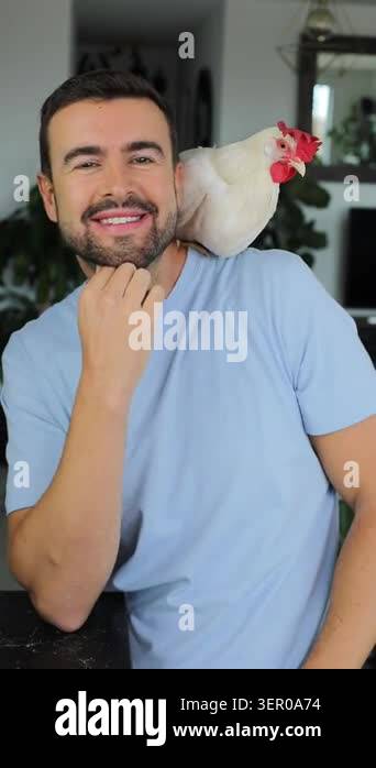 Vertical video showing a smiling man with a white chicken perched on ...