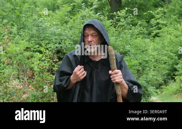 Monk in dark clothing holds a wooden staff and walks through a green ...