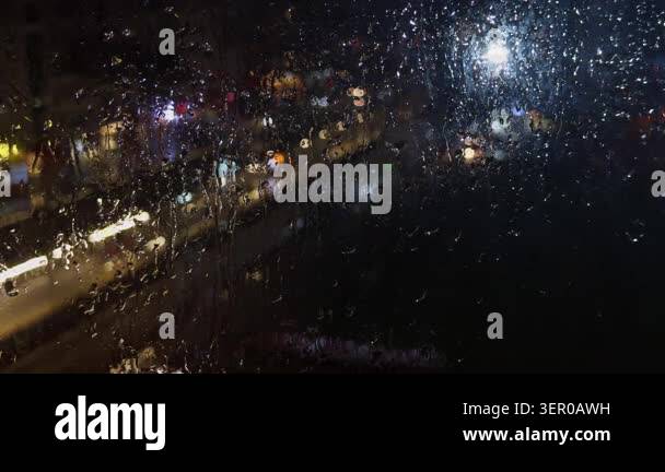 Glistening raindrops on a glass window against a vibrant bokeh of city ...