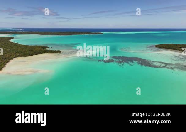 Turquoise lagoon beach with anchored boat, lush pine and palm fringe ...