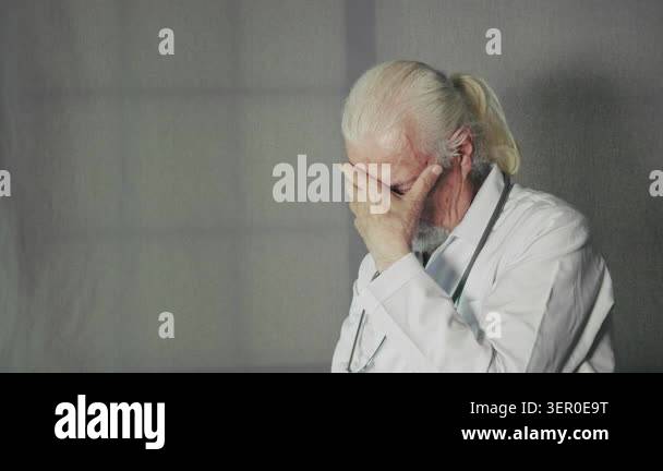 Exhausted senior male doctor looking tired after a long shift in a ...