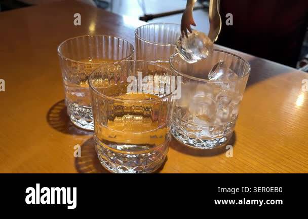 Ice cubes drop into clear glass creating refreshing splash while bottle ...