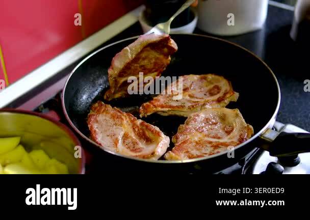 A hot pork steak sizzles in a frying pan as male hands turn the meat ...