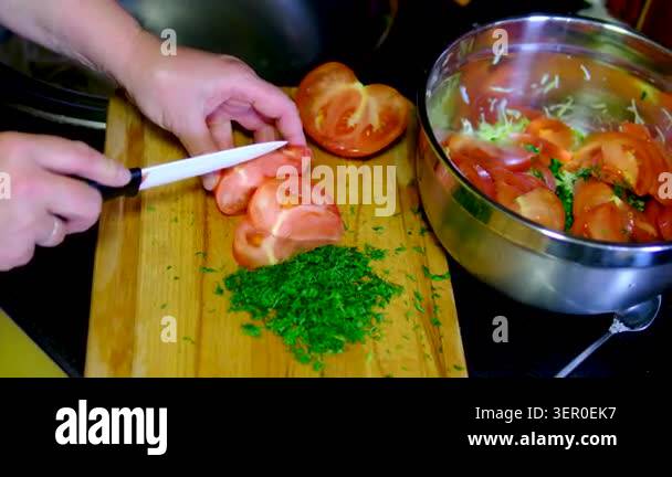 Dill and pink tomato are being cut on a board, a salad is being ...