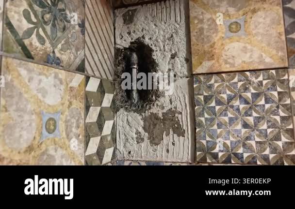 Slow push in toward damaged mosaic tile wall revealing exposed copper ...