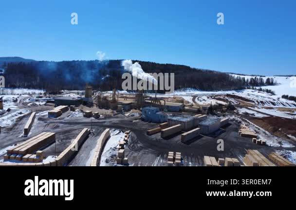 Industrial sawmill aerial shot in winter featuring lumber kilns, smoke ...