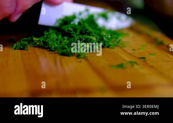 Chopping fresh herbs on wooden board with kitchen knife Chop dill on a ...