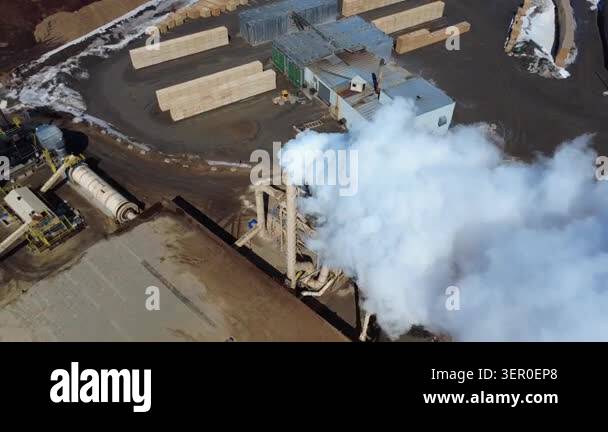 Drone orbit around a steaming sawmill chimney, revealing lumber piles ...