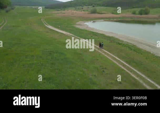 Drone view of two people walking along a rural dirt road beside a ...