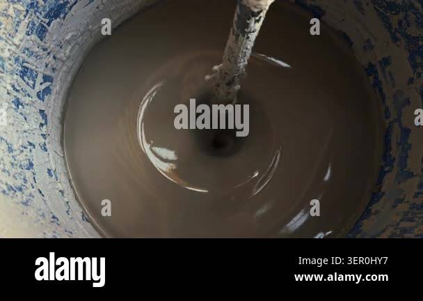 Close-up of liquid clay mud swirling in an industrial mixer within a ...
