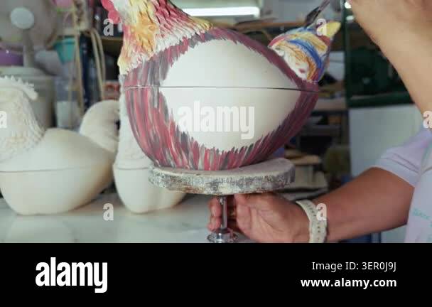 Close up of an artisan hand painting a handmade ceramic chicken ...