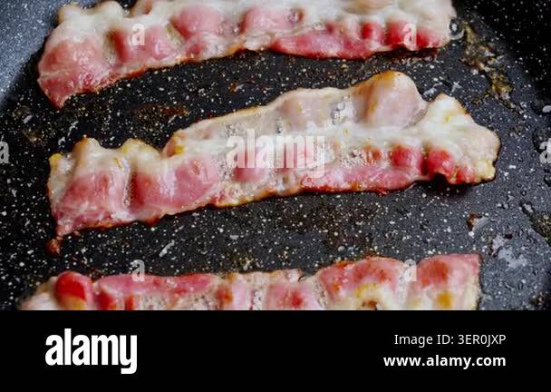 Cooking bacon until golden with crispy edges. Sizzling bacon slices ...