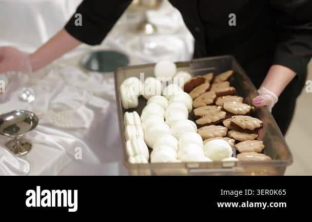 Catering staff in gloves holding a tray of white macarons and shell ...