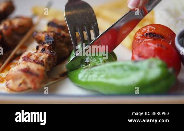 Person cuts green pepper and grilled meat on a plate with sides Stock ...