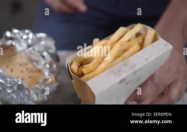 A person takes fries from a box while holding a burger nearby Stock ...