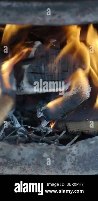 Bright flames rise from burning wood in a charcoal fire pit outside ...