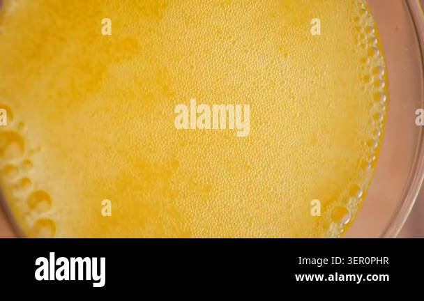 Fresh juice is being mixed in a clear glass bowl with bubbles forming ...