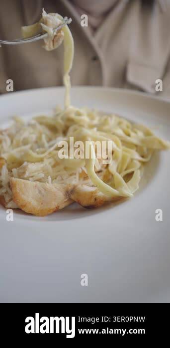 A person eats pasta with chicken and cheese on a plate at a restaurant ...
