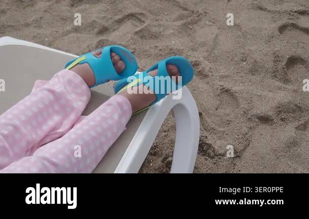 A child rests on a beach chair while sand surrounds their feet Stock ...