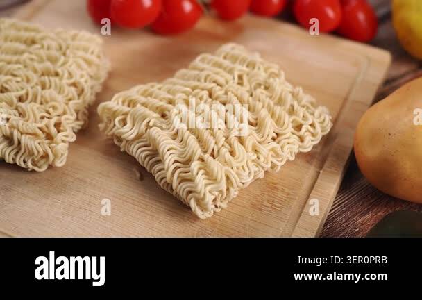 Noodles are placed on a cutting board alongside fresh tomatoes and ...