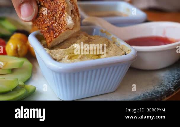 A hand dips bread into hummus while enjoying fresh vegetables Stock ...