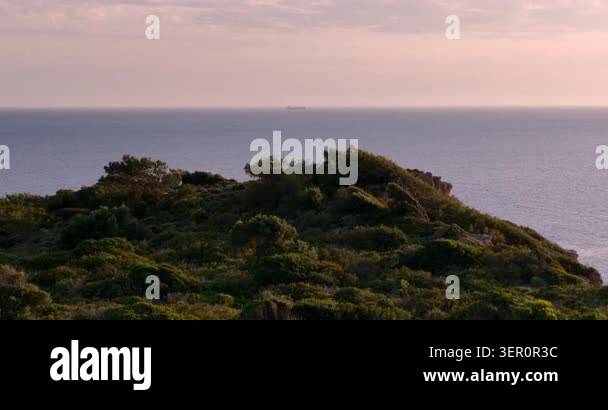 Drone footage reveals a lush green hilltop promontory overlooking calm ...