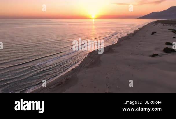 Aerial view tracks along an empty sandy shoreline as gentle waves roll ...