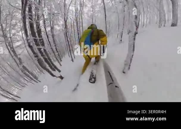Solo skier in yellow jacket ascending steep snow covered slope through ...