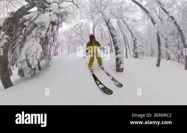 Solo skier in yellow jacket ascending steep snow covered slope through ...