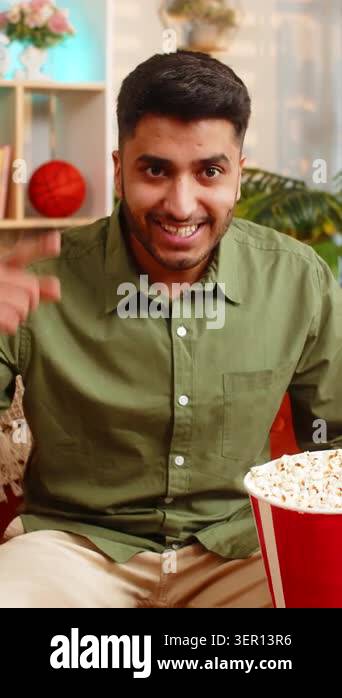 Indian man on home sofa watches sports match with popcorn raises fist ...