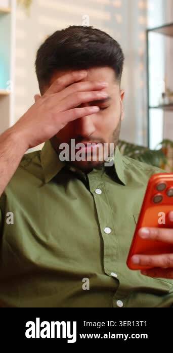Indian man on home sofa reads smartphone news with sad shock holding ...