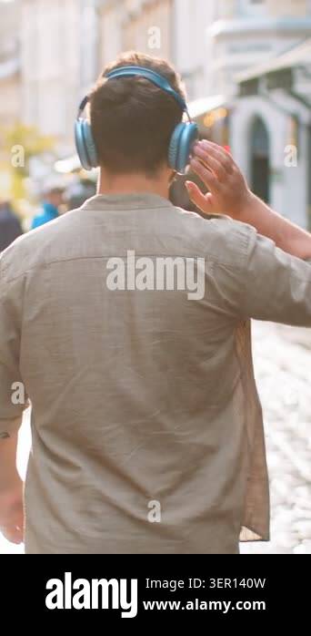 Rear view of man tourist in wireless headphones walking through the ...