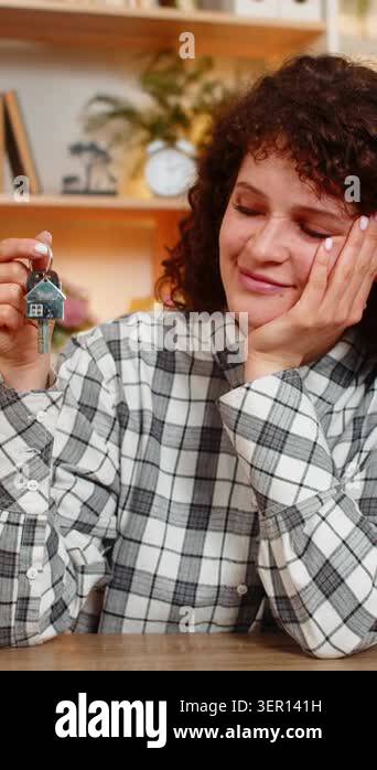 Young woman on home table holds apartment keys and smiles with pride ...
