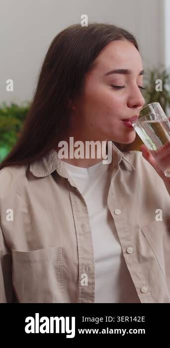 Thirsty young woman holding glass of natural aqua make sips drinking ...