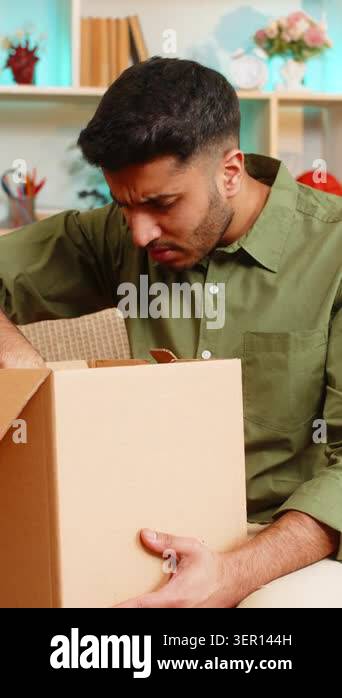 Indian man on home sofa opens delivery box and frowns at wrong order ...