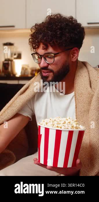 Arabian man at home watches movie on tv holds popcorn laughs comments ...
