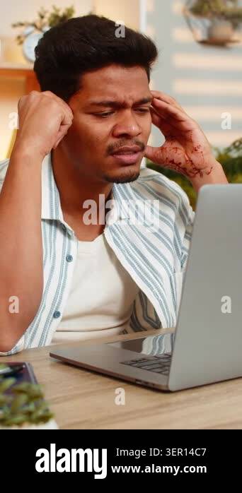 Indian man on home table looks at laptop screen with focused mind while ...