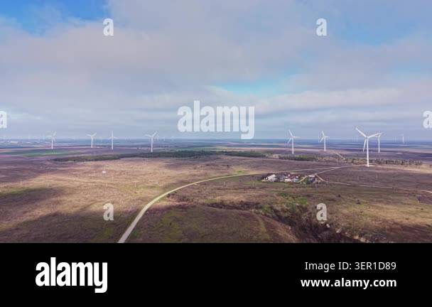 Wind turbines rotate in a wide flat area. A road leads towards a small ...