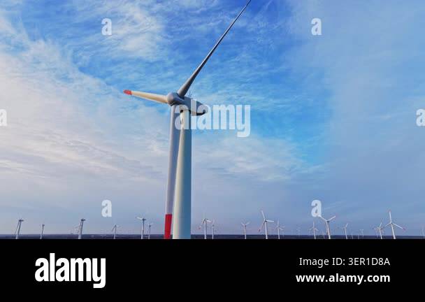 Wind turbines spin above the ocean at a wind farm during the day. The ...