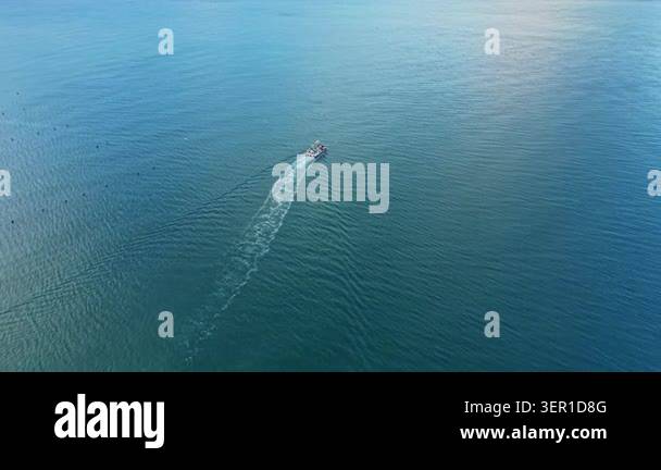 A small boat moves across the clear blue water with light waves. The ...