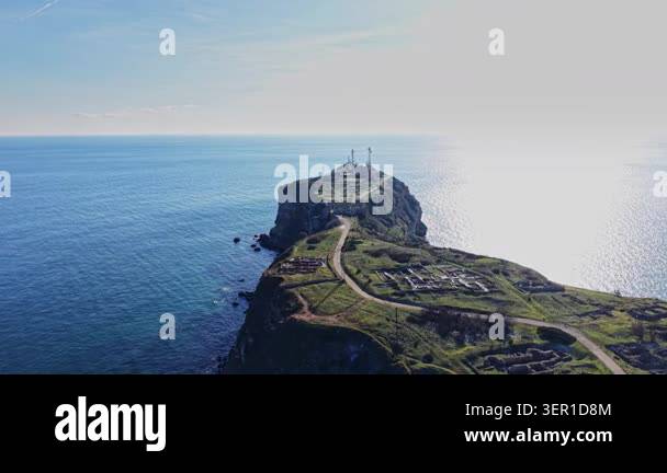 A coastline with a cliff that has a lighthouse at the top. There are ...