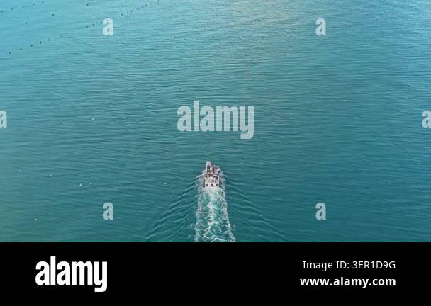 A boat moves through clear blue water under a bright sky. The wake ...