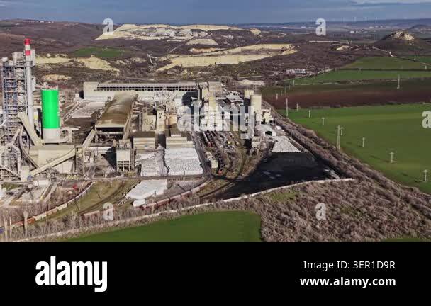 A factory is seen in a rural area surrounded by green fields and hills ...