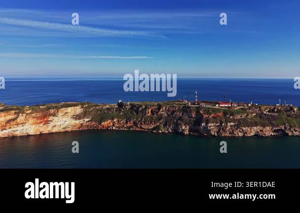 A cliff by the sea with a clear sky overhead. The coastline features a ...