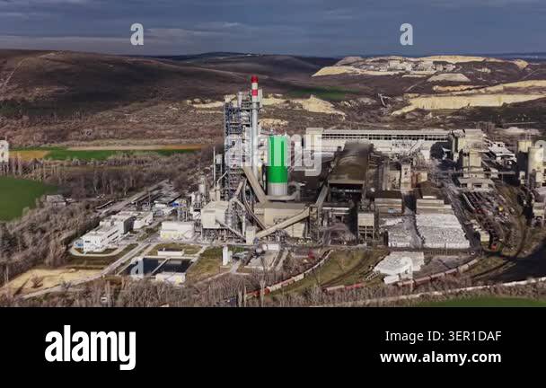 An industrial facility with a prominent green tower surrounded by hills ...