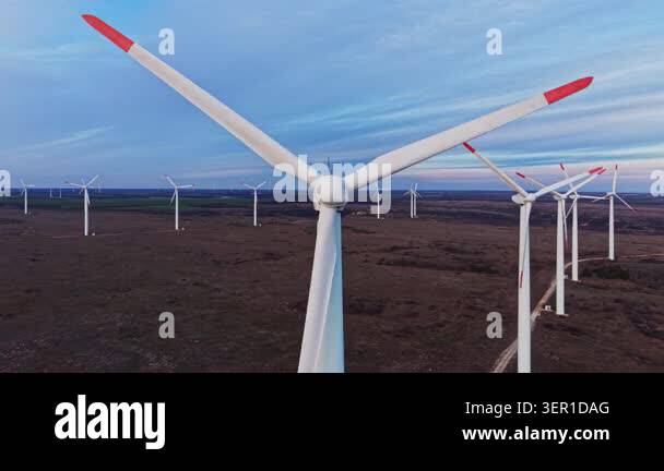 Wind turbines rotate in a wide-open field as the sun sets in the ...