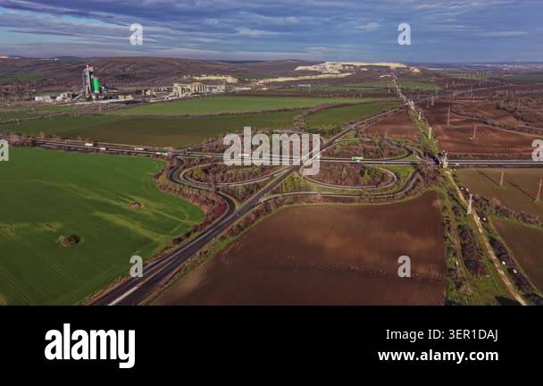 Vehicles travel on a highway surrounded by fields and hills. An ...