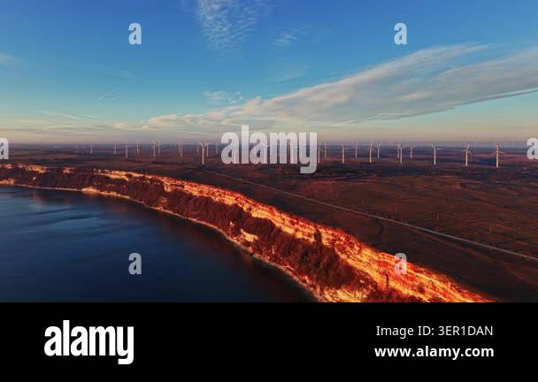 Wind turbines stand on the horizon near a rocky cliff. Waves crash on ...